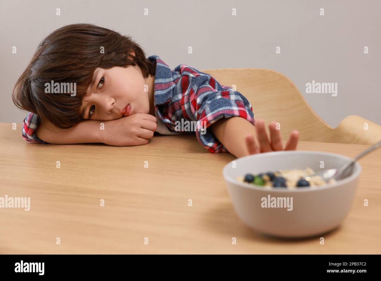 Cute little boy refusing to eat his breakfast at table on grey ...
