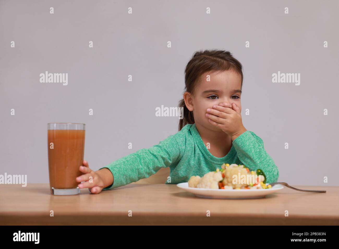 Cute little girl covering mouth and refusing to drink juice at table on ...
