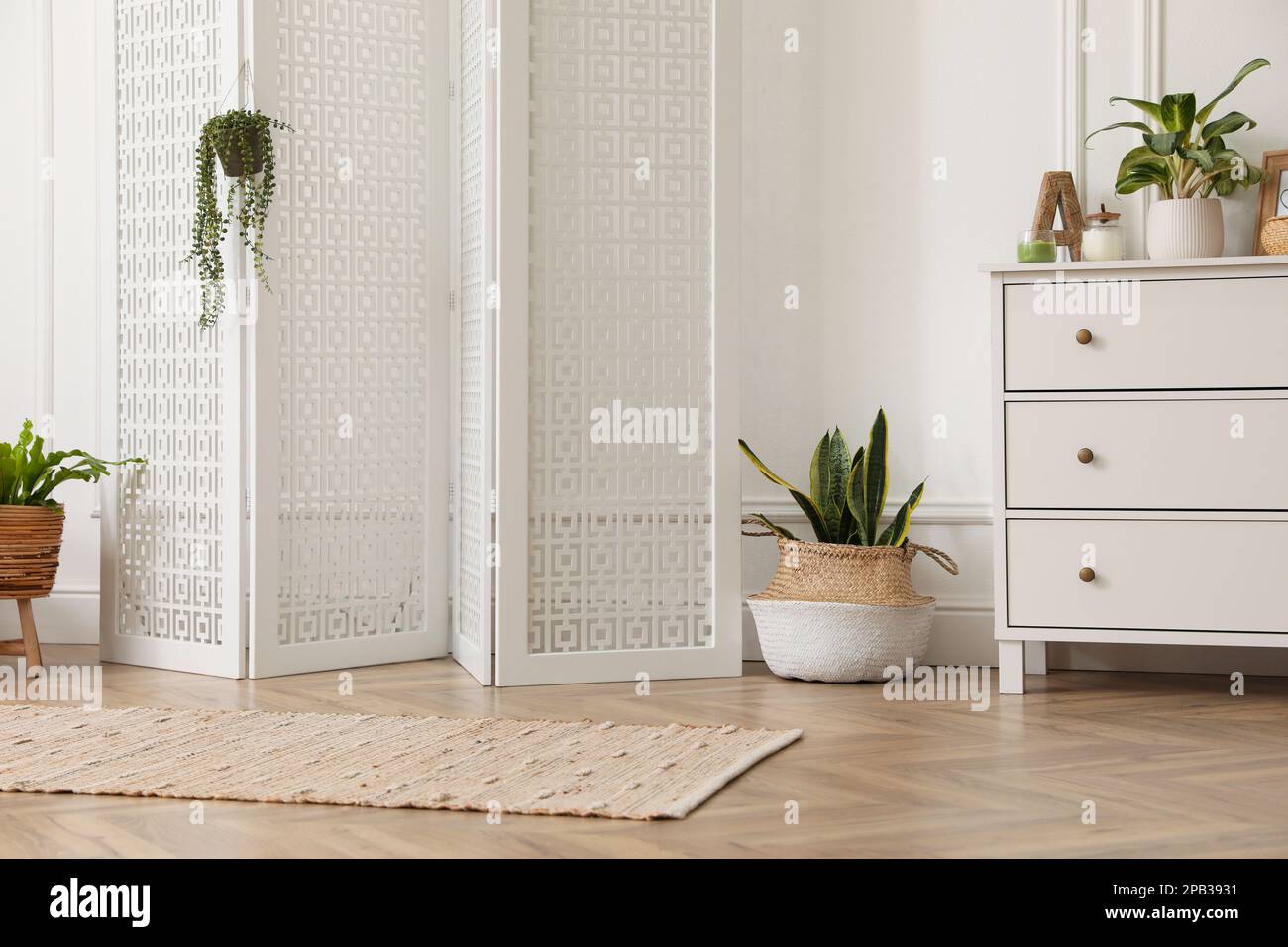 Stylish room with wooden folding screen and chest of drawers near white ...