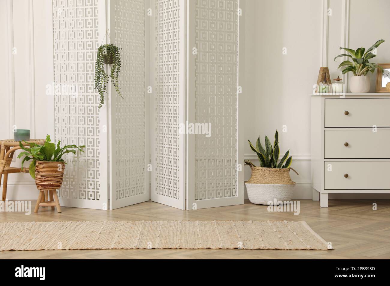 Stylish room with wooden folding screen and chest of drawers near white ...