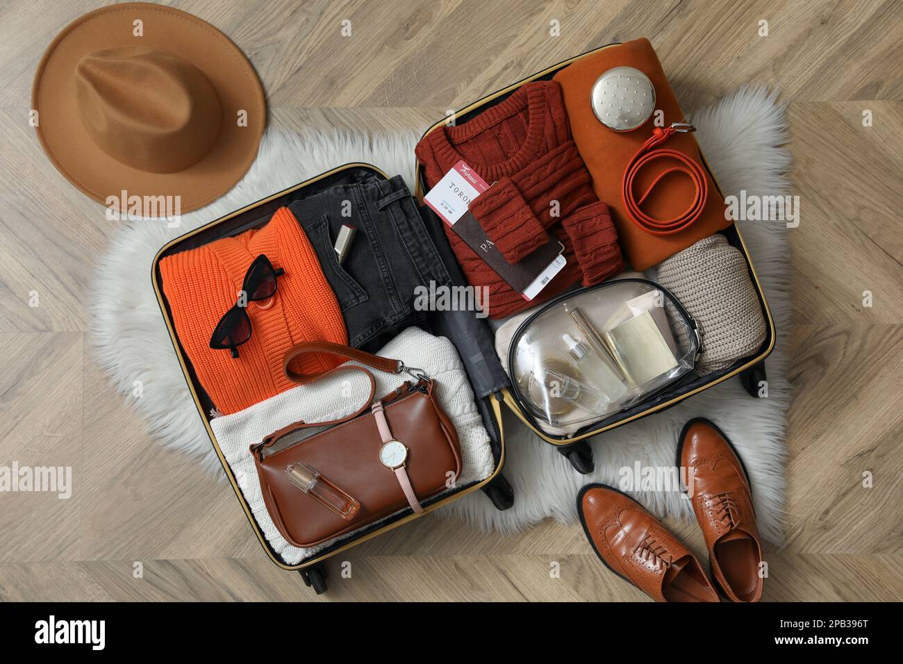 Open suitcase with folded clothes, accessories and shoes on floor, flat ...