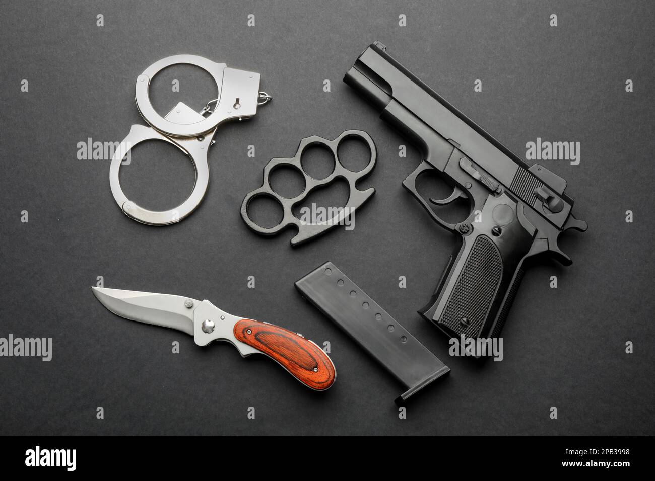 Brass knuckles, gun, knife and handcuffs on black background, flat lay ...