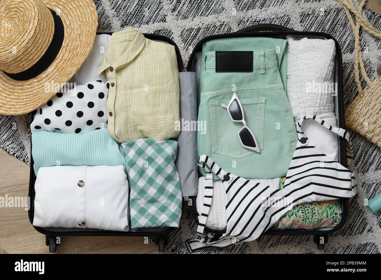 Open suitcase with summer clothes and accessories on floor, flat lay ...