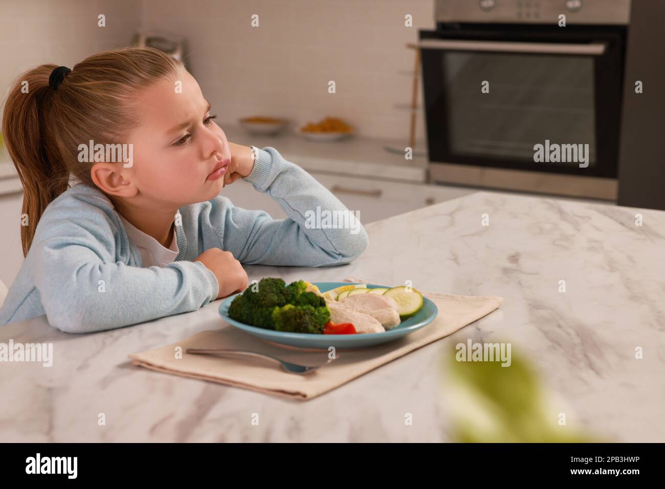 Cute little girl refusing to eat dinner in kitchen, space for text ...