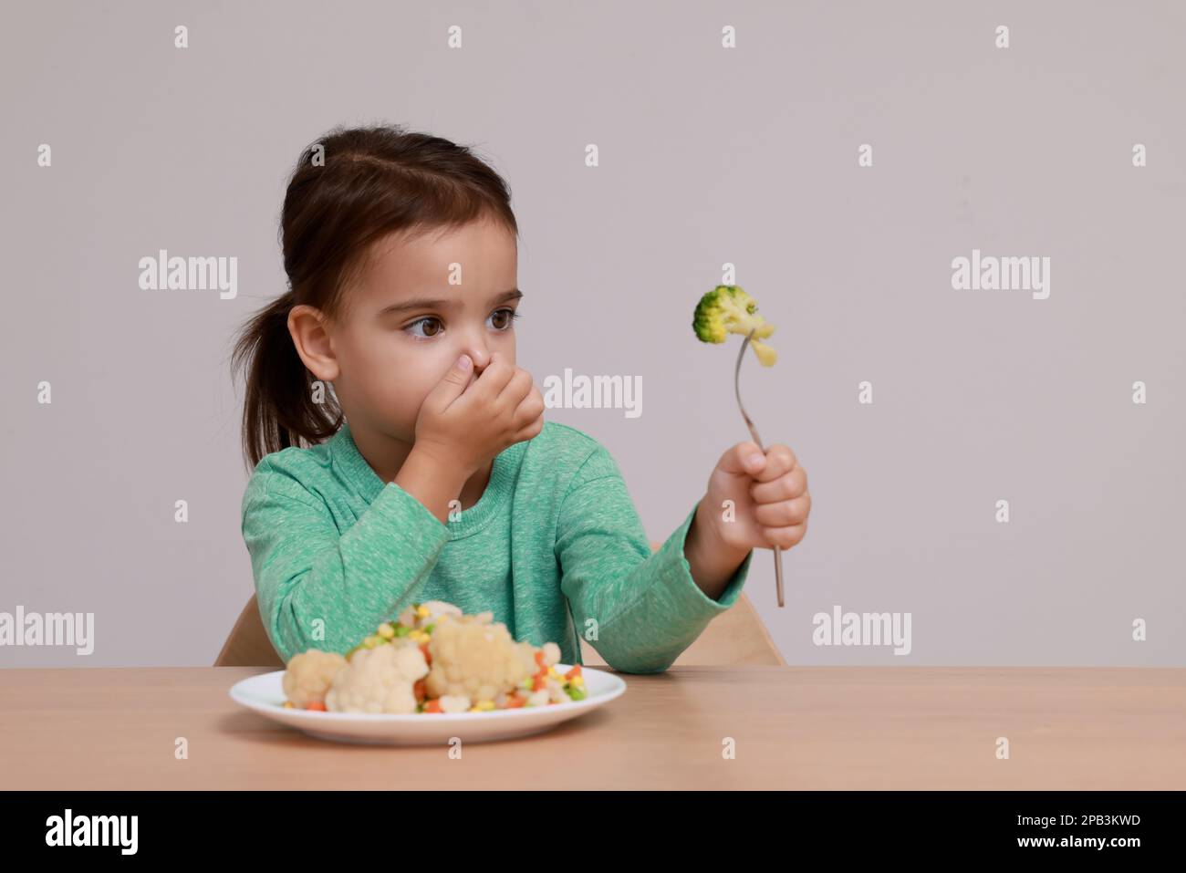 Cute little girl closing nose and refusing to eat vegetable salad at ...