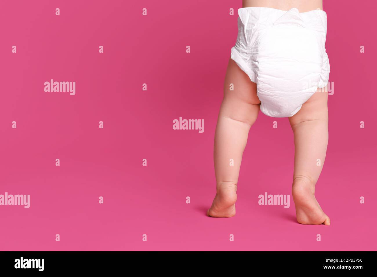 Back view of cute baby in dry soft diaper standing on pink background ...