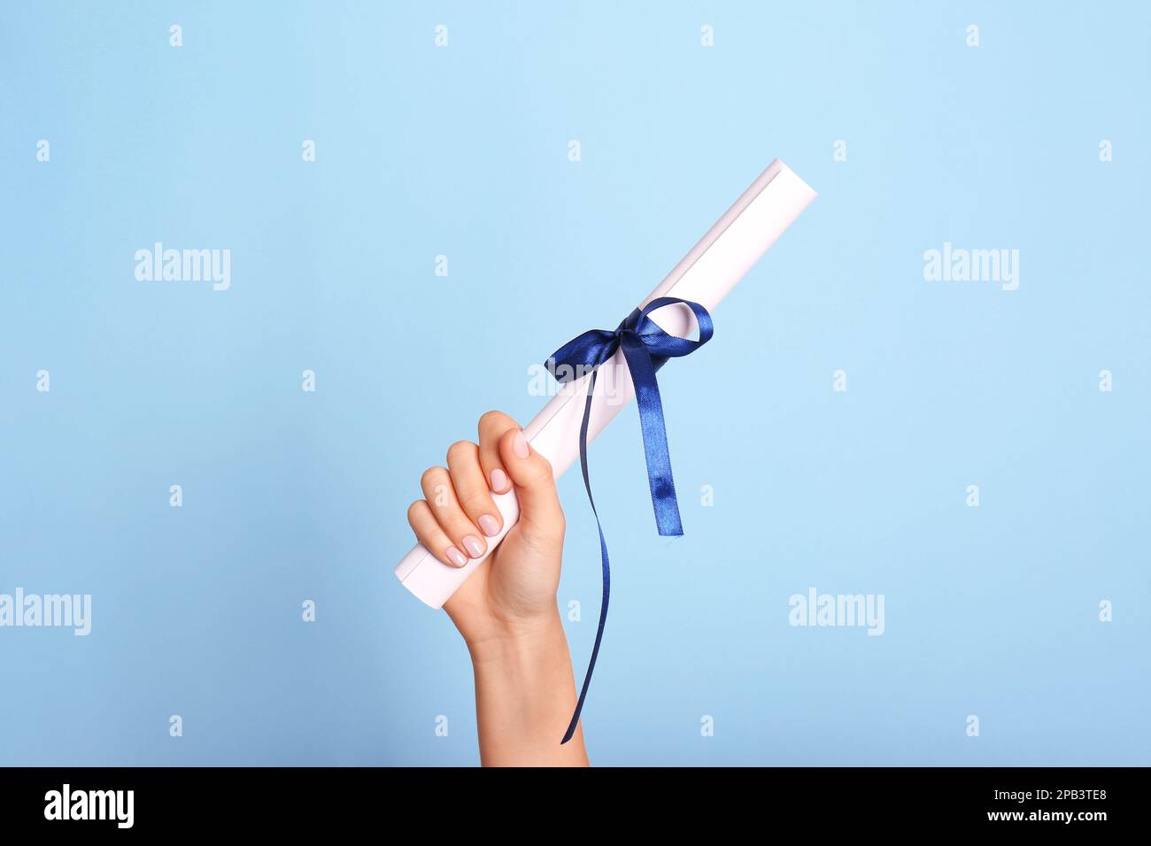 Student holding rolled diploma with ribbon on light blue background ...
