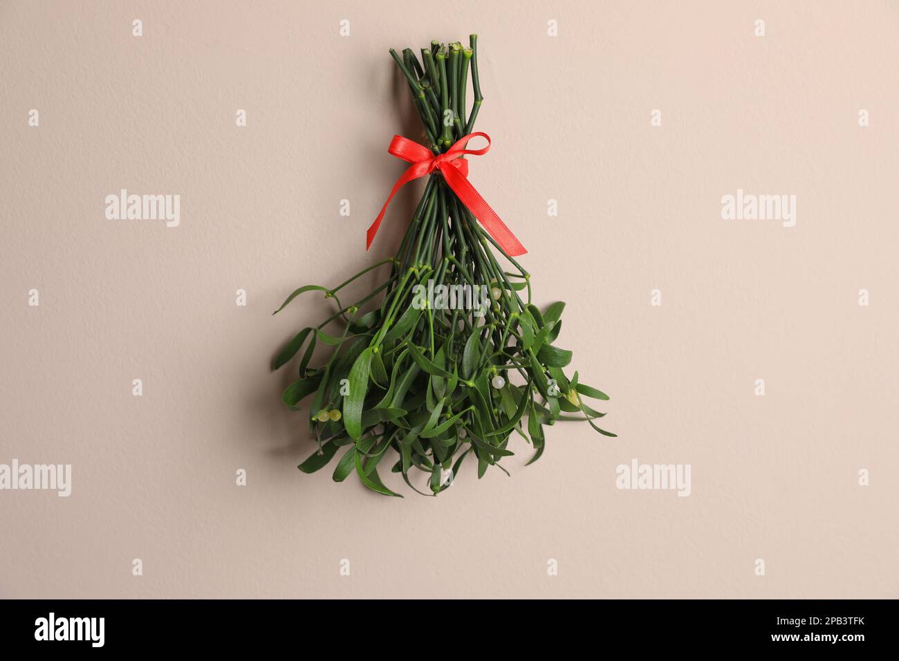 Mistletoe bunch with red bow on beige table, top view. Traditional ...