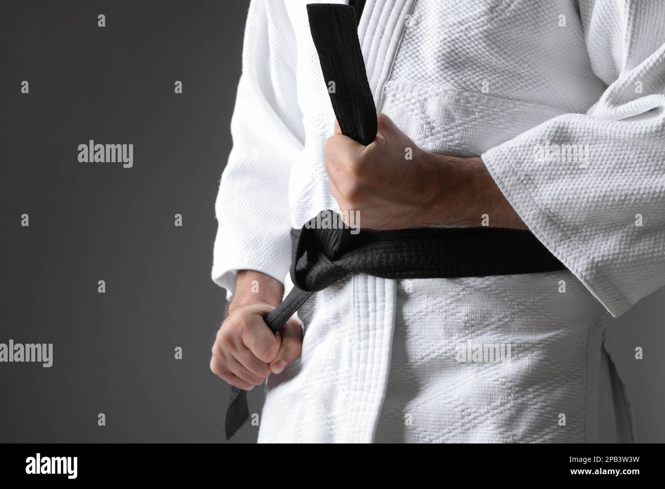 Karate coach wearing kimono and black belt on grey background, closeup ...