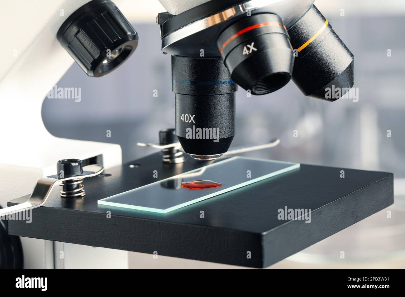 Glass slide with sample of red liquid under microscope in laboratory ...
