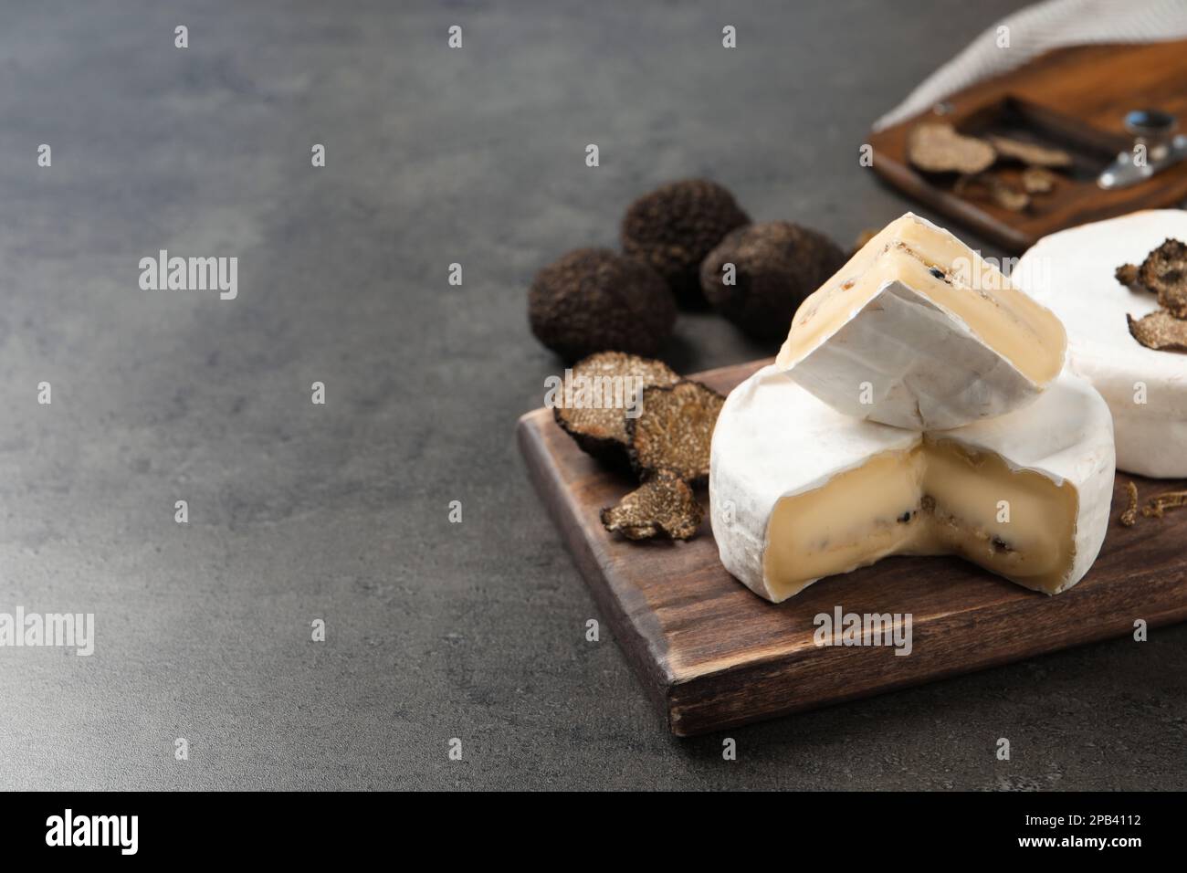 Wooden board with delicious truffle cheese on grey table. Space for ...
