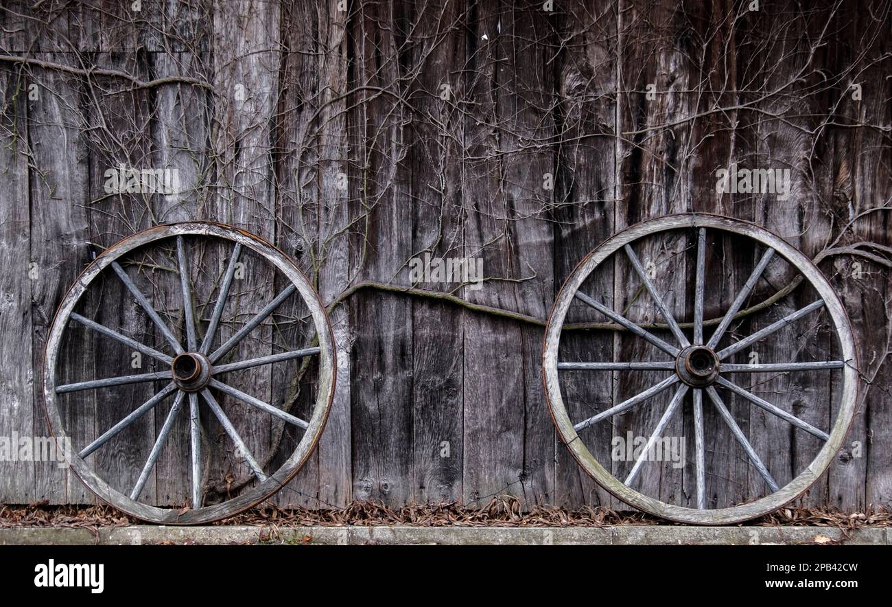 Two wagon wheels leaning against a barn wall Stock Photo - Alamy