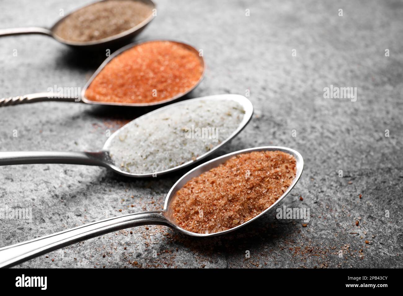 Spoons with different kinds of salt on grey table Stock Photo - Alamy