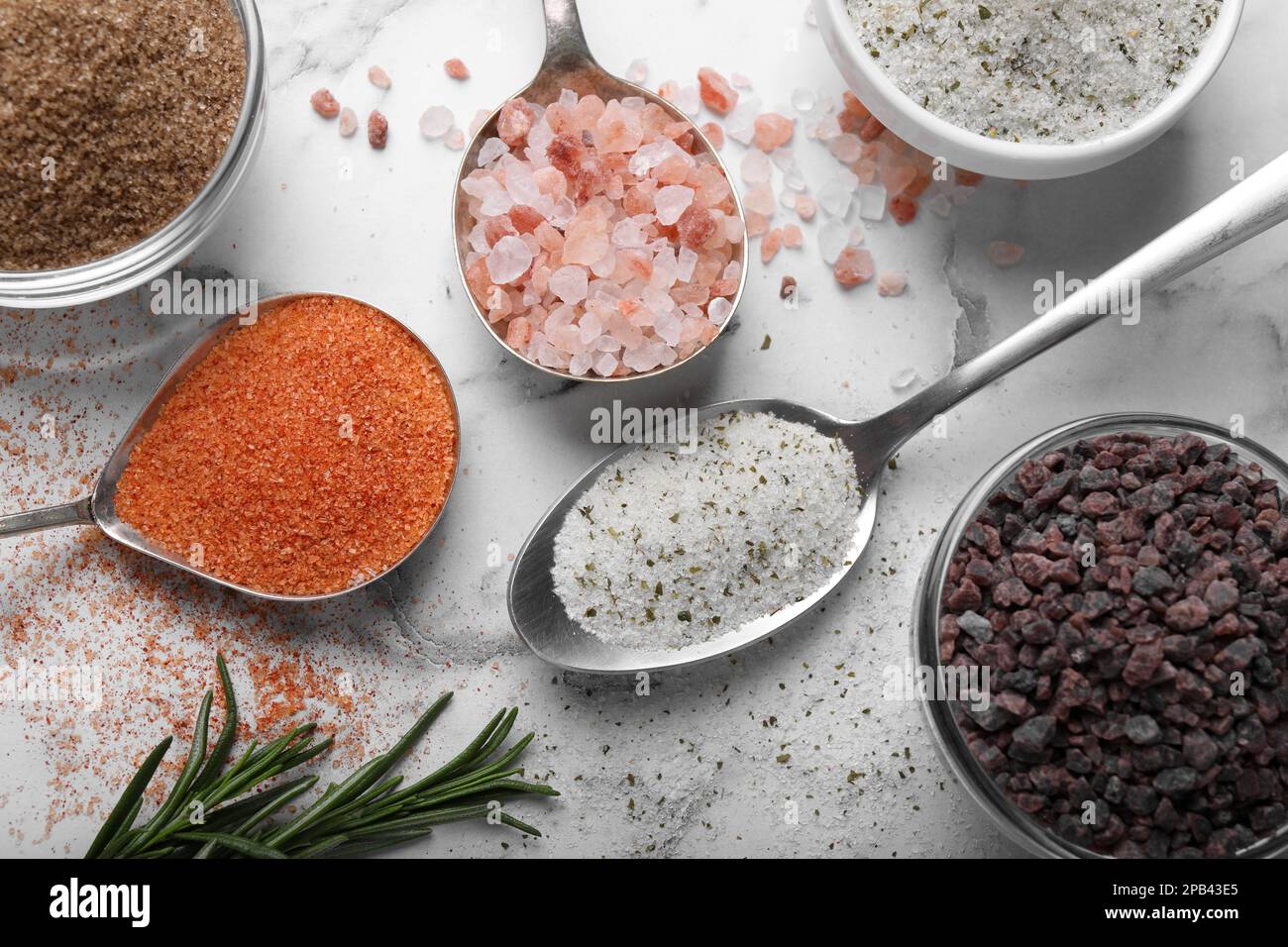 Flat lay composition with different kinds of salt on white marble table ...