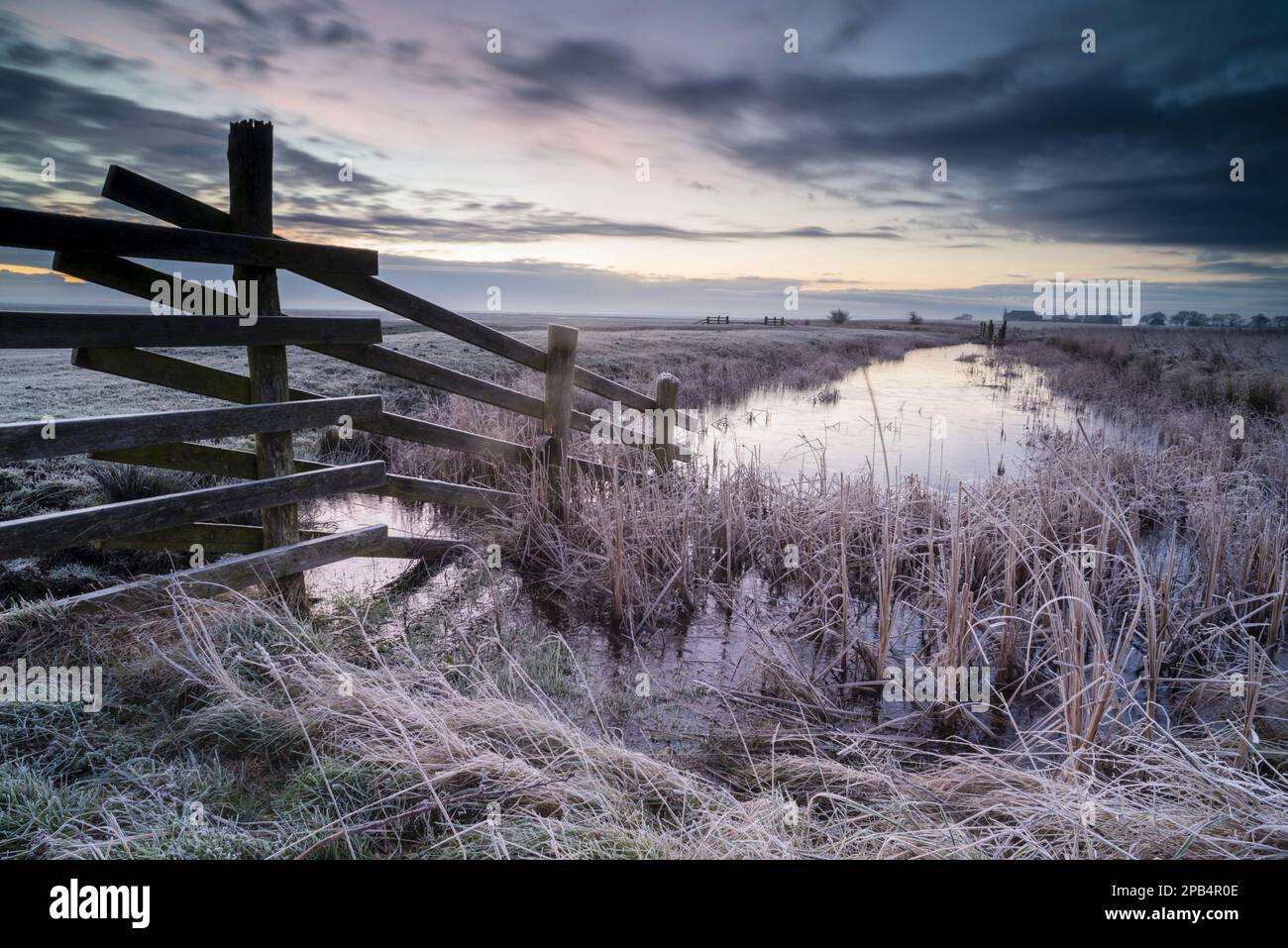Cattle fence leading into ditch on frost-covered pasture at dawn ...