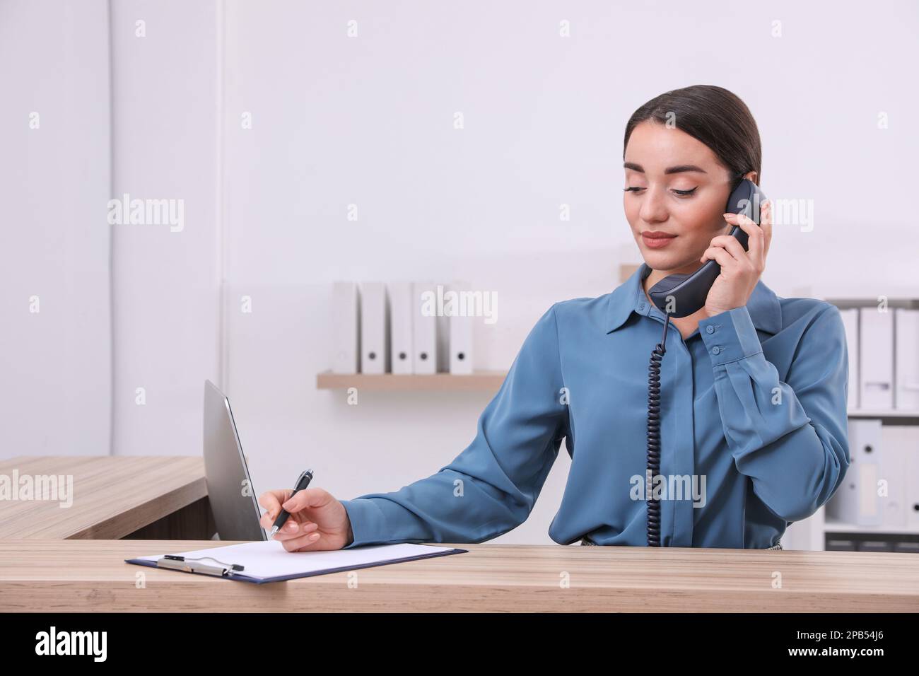 Female receptionist with clipboard talking on phone at workplace Stock ...