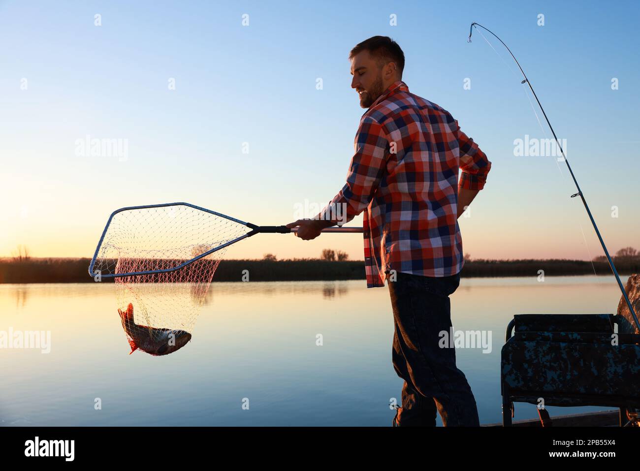 Fisherman holding fishing net with catch at riverside Stock Photo - Alamy
