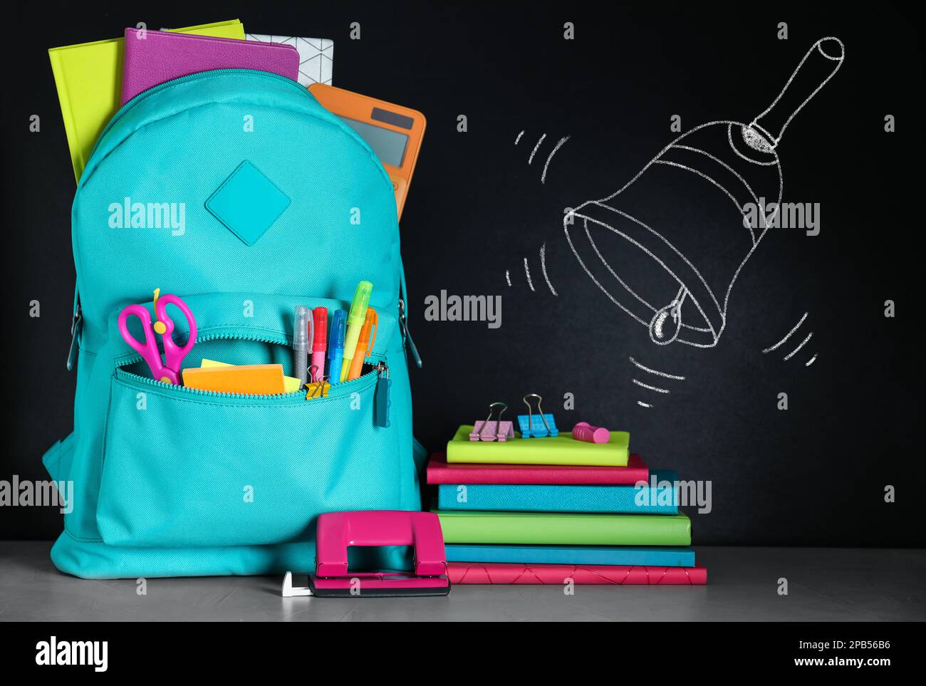 Backpack full of stationery near blackboard with drawn school bell ...