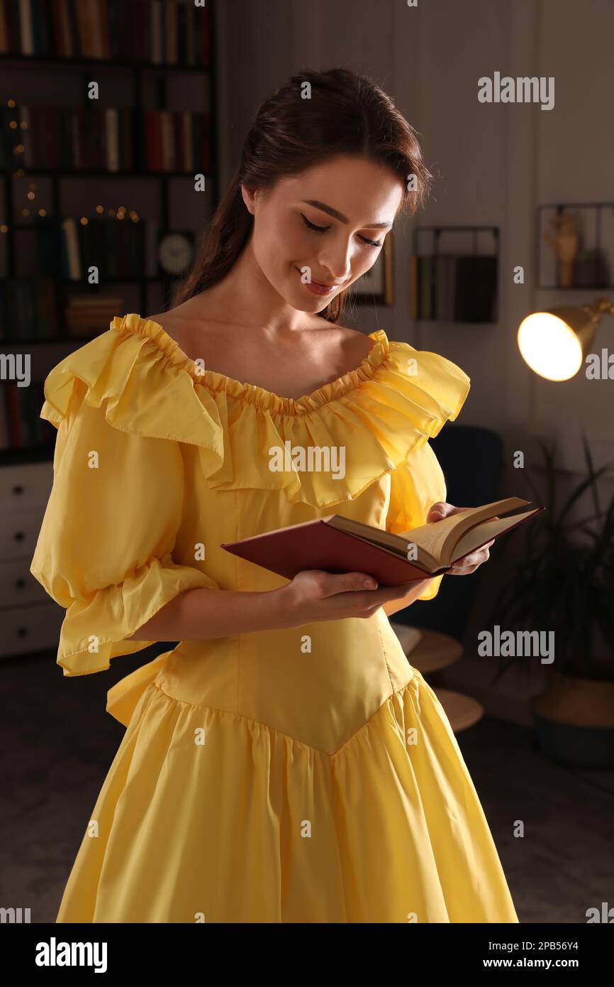 Beautiful young woman in yellow dress reading book at home Stock Photo ...