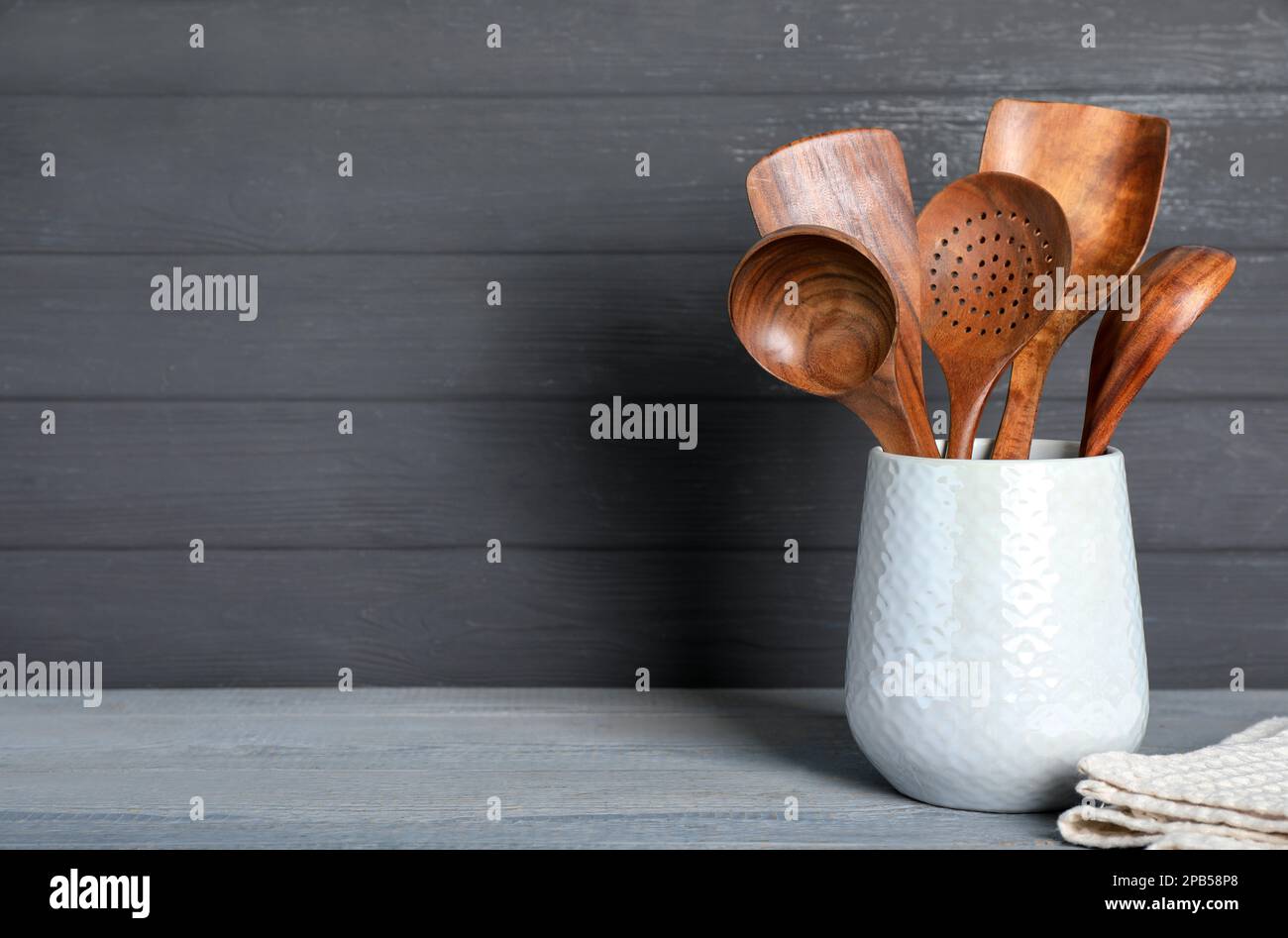 Set of kitchen utensils in holder on grey wooden table, space for text ...