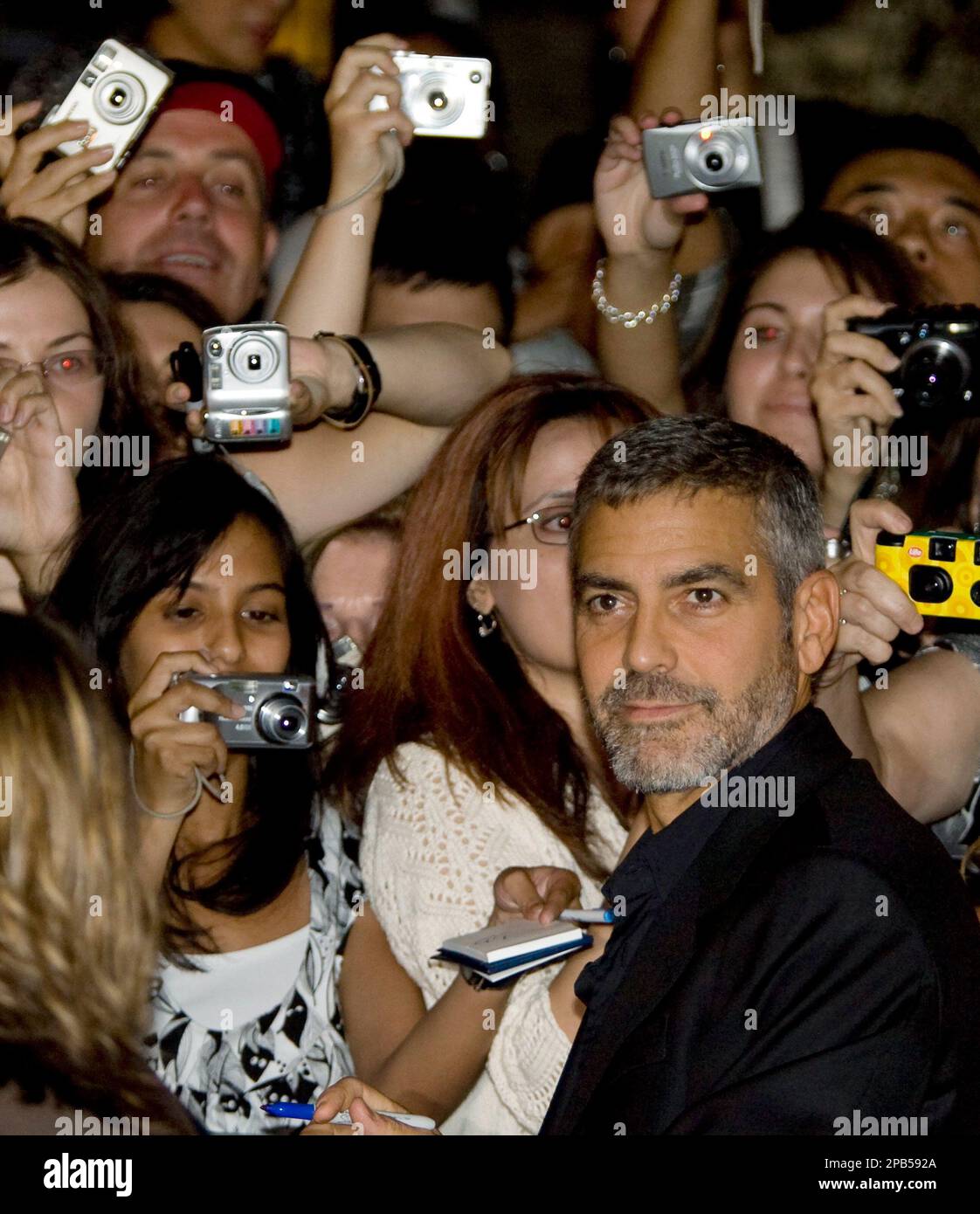 George Clooney turns around as fans take photos of him while he signs ...