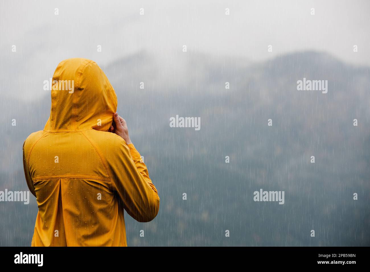 Woman in raincoat enjoying mountain landscape under rain, back view ...
