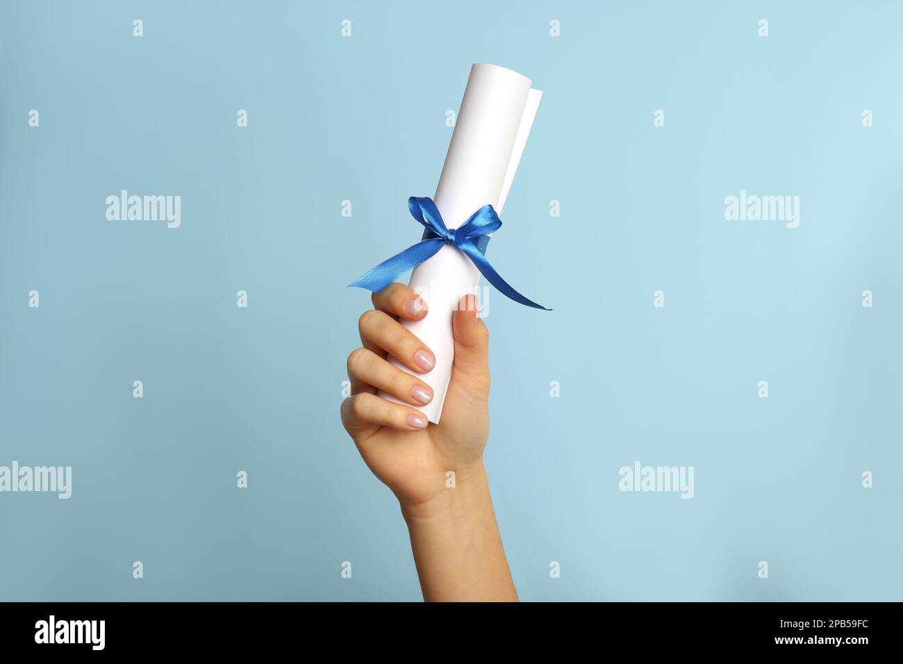 Student holding rolled diploma with ribbon on light blue background ...