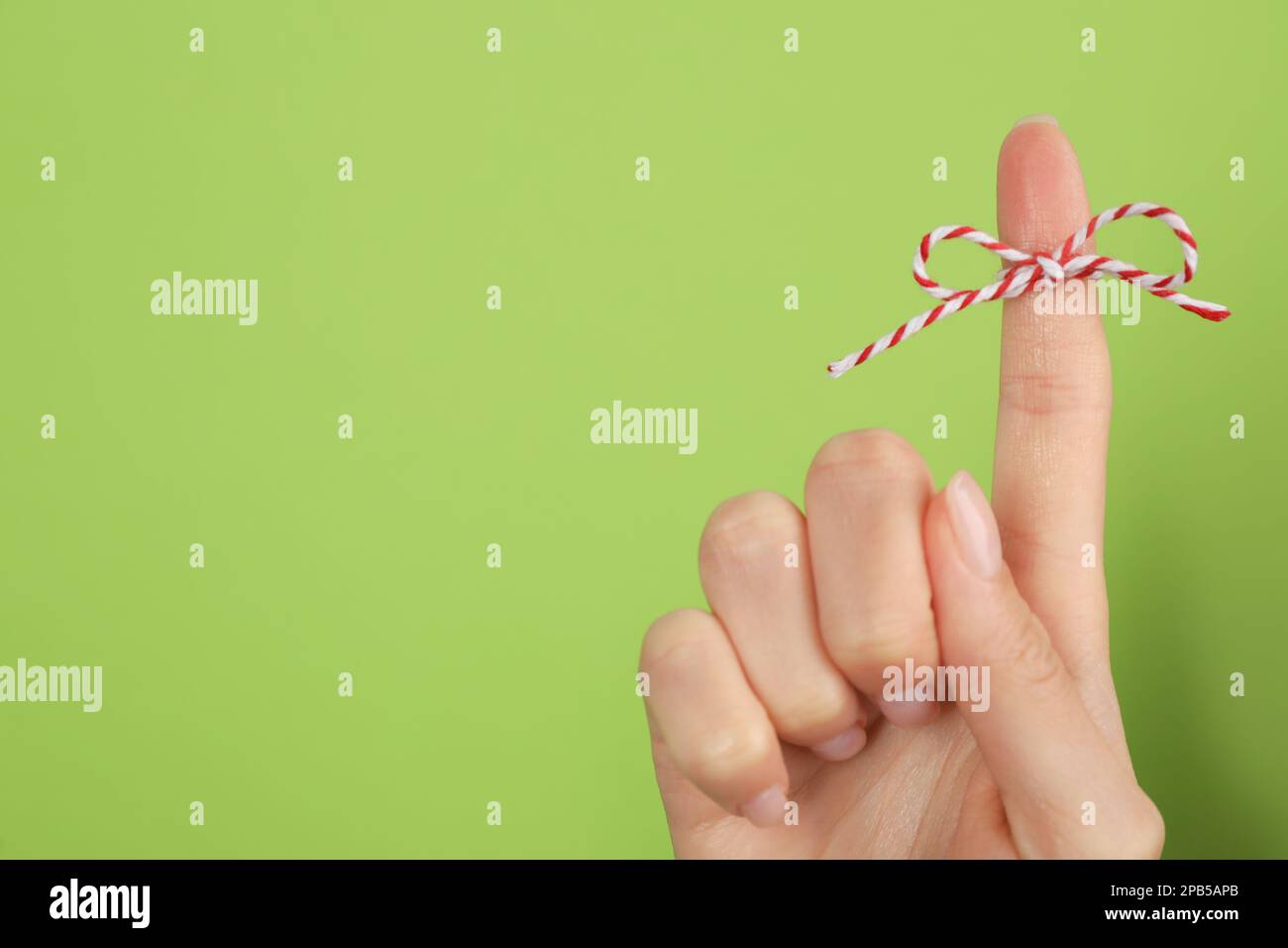 Woman showing index finger with tied bow as reminder on light green ...
