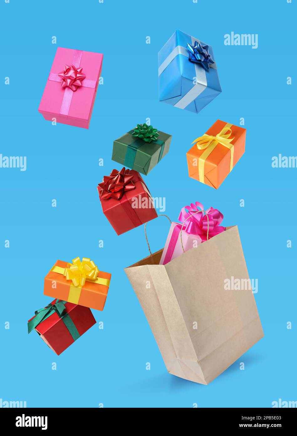 Many different gift boxes falling into paper shopping bag on light blue ...