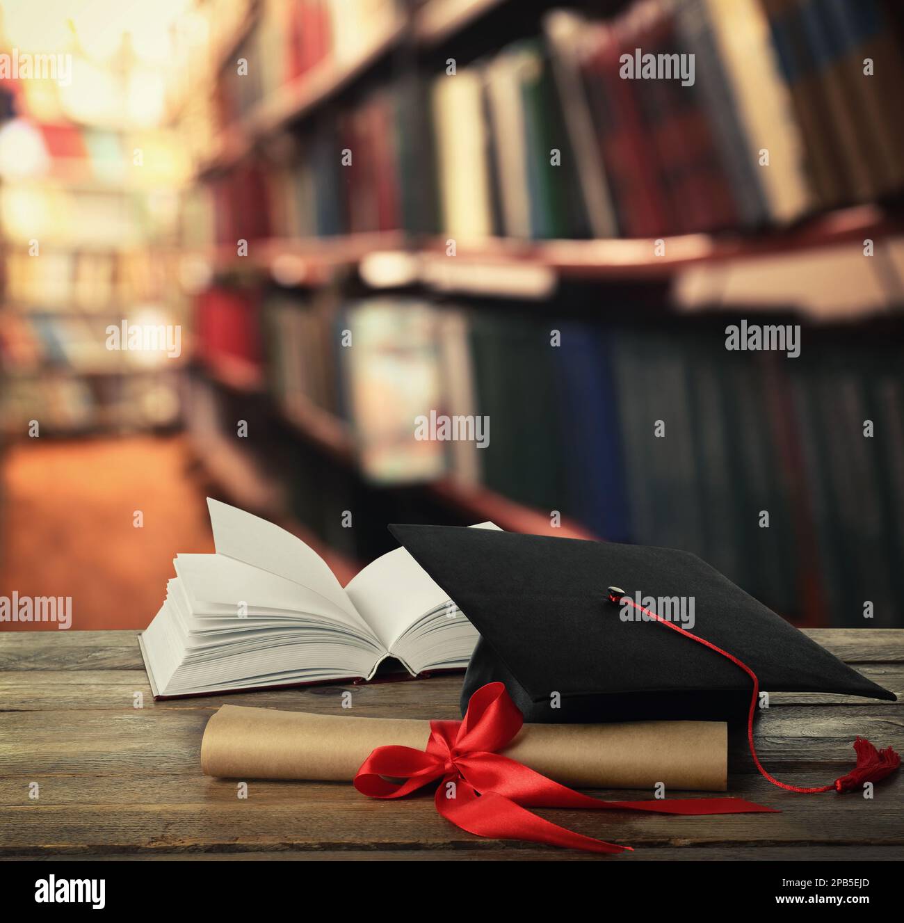 Graduation hat, book and diploma on wooden table in library Stock Photo ...