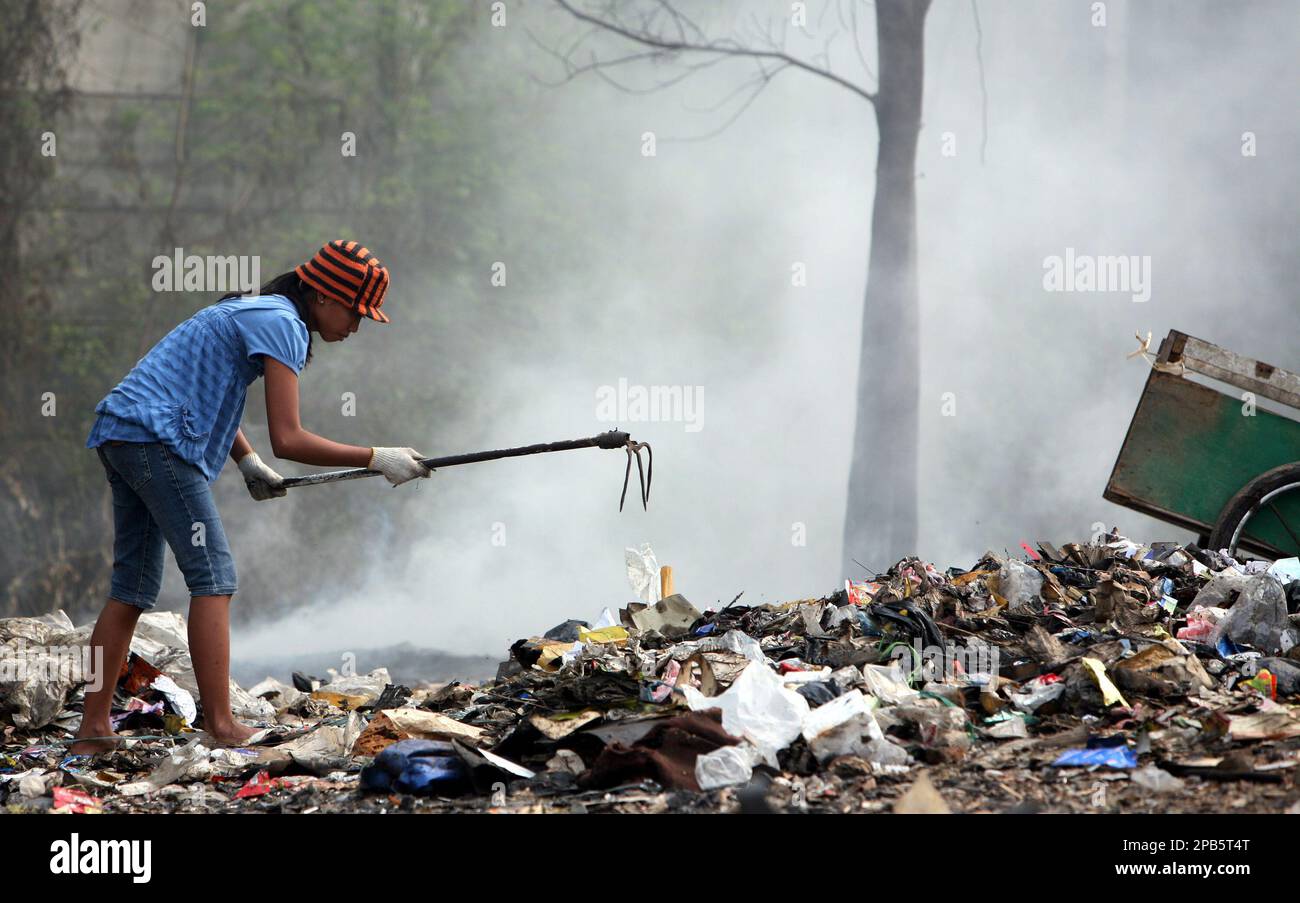 A scavenger women picks through trash at garbage dump in the outskirts ...