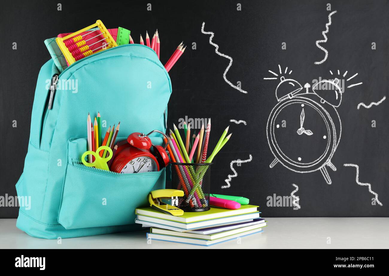 Backpack full of stationery near blackboard with drawn alarm clock ...