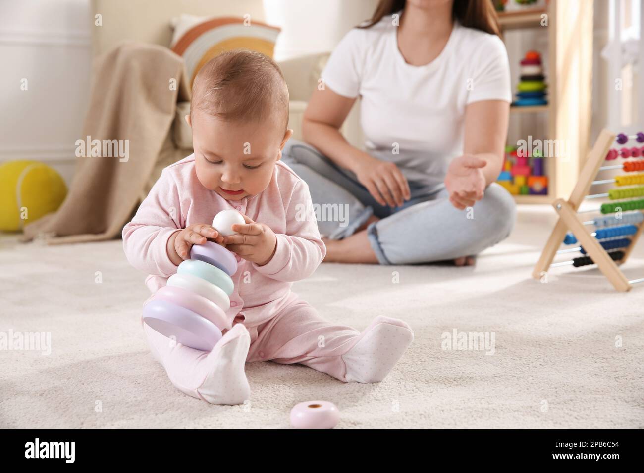 Cute baby girl playing with toy pyramid and mother on floor at home ...
