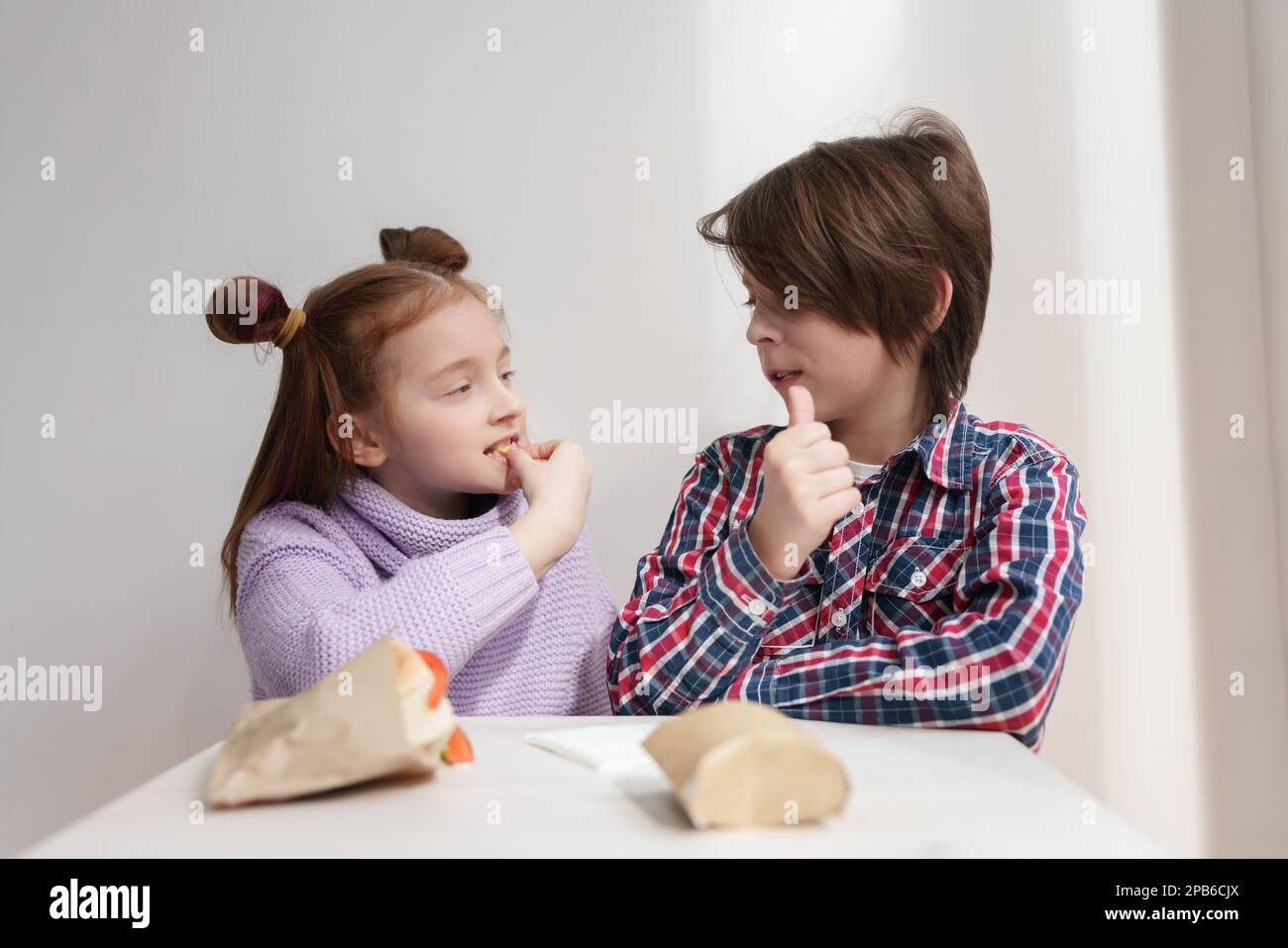 Cute white kids looking at each other while eating fries in a fast food ...
