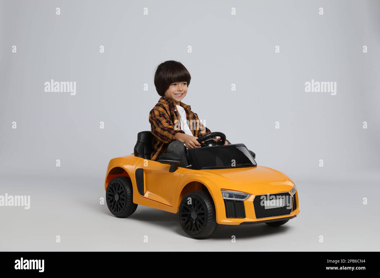 Cute little boy driving children's electric toy car on grey background ...