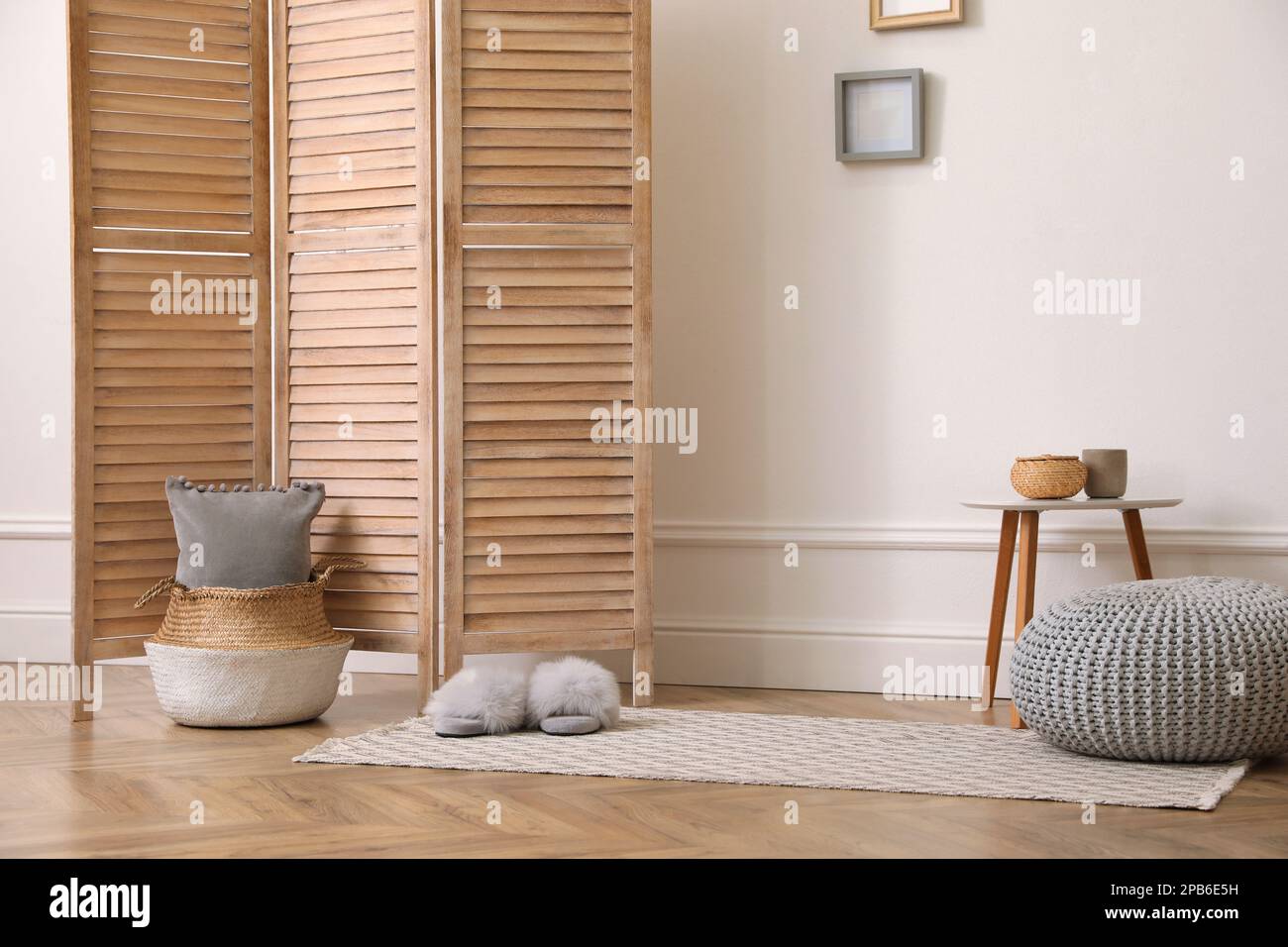 Folding screen, small table and knitted pouf near white wall in room ...