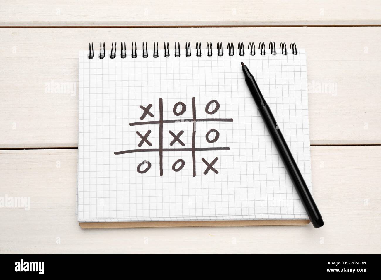 Notebook with tic tac toe game and marker on white wooden table, top ...