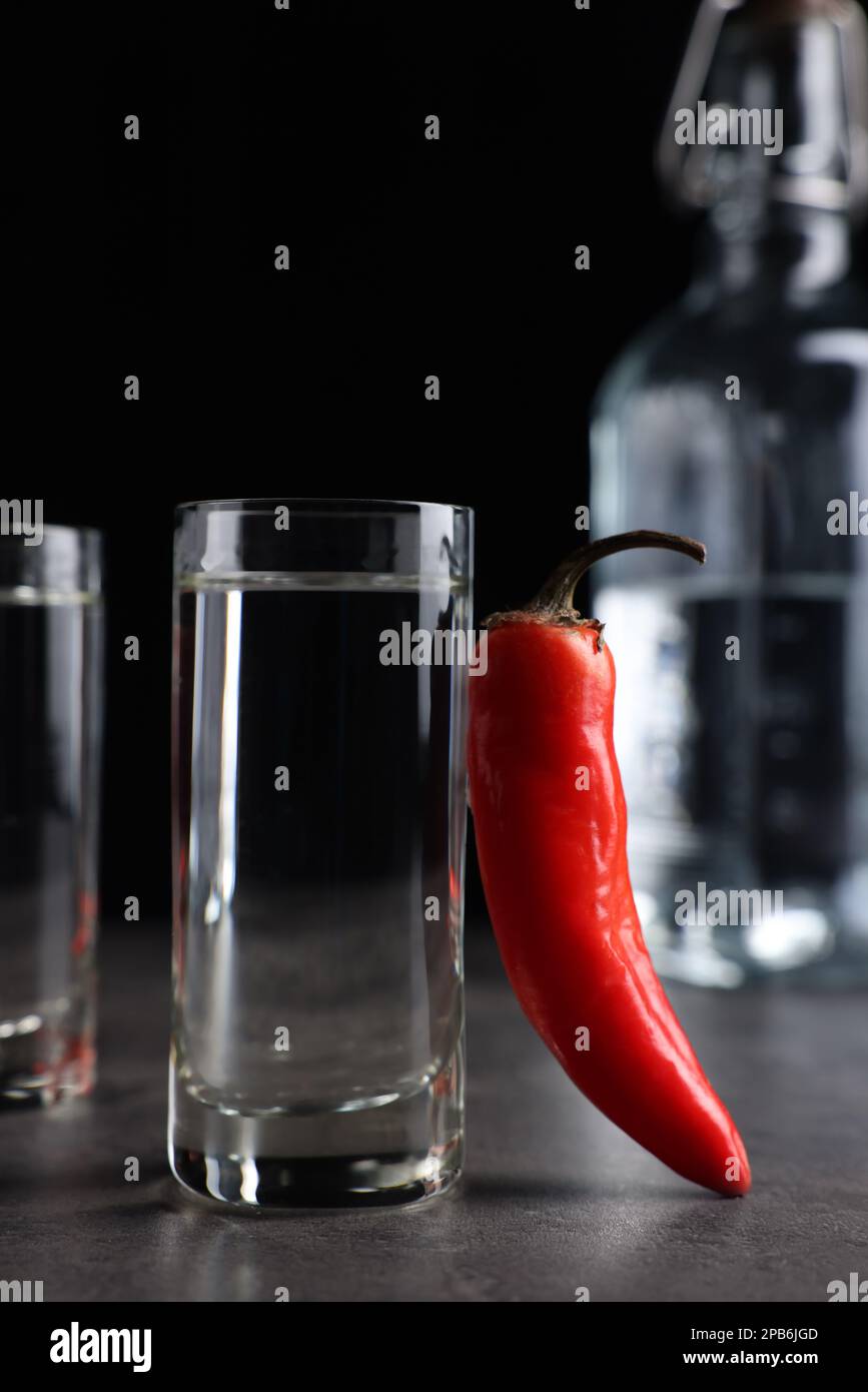 Red hot chili pepper and vodka on grey table against black background ...