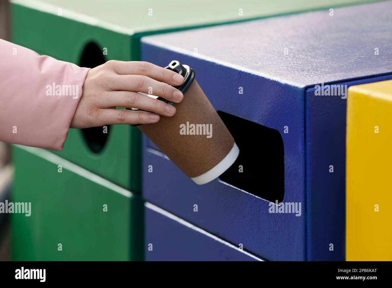 Woman throwing paper coffee cup into garbage bin outdoors, closeup ...