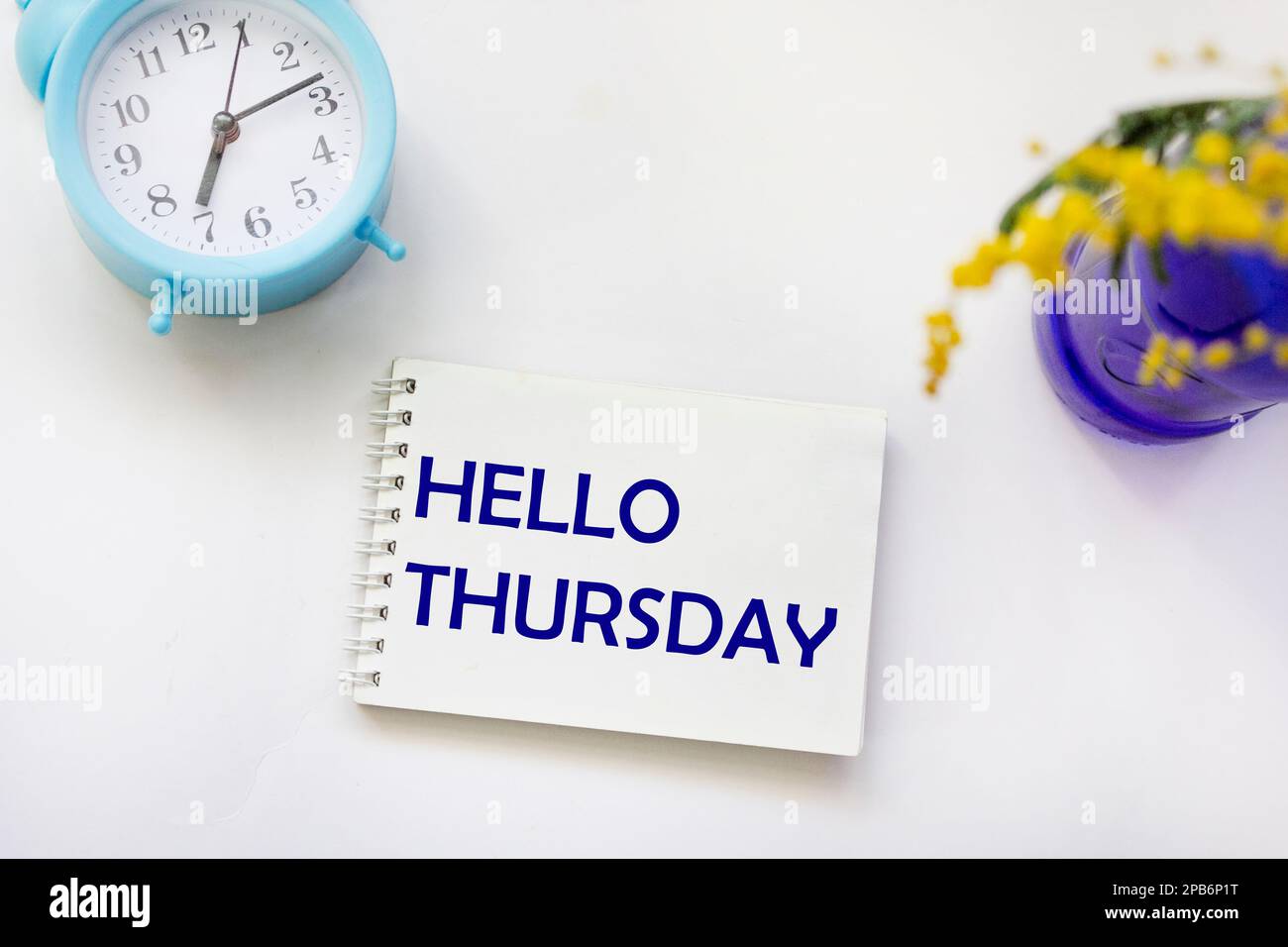 Hello Thursday words on a notepad and a bouquet of mimosa flowers in a ...