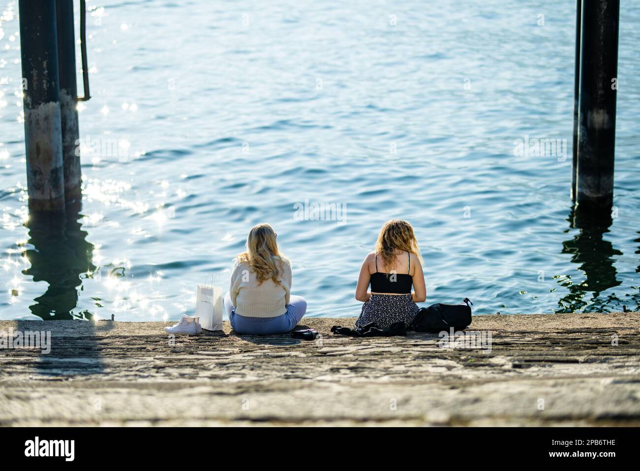 BELLAGIO, ITALY - APRIL 2022: Two young women sitting at the embankment ...