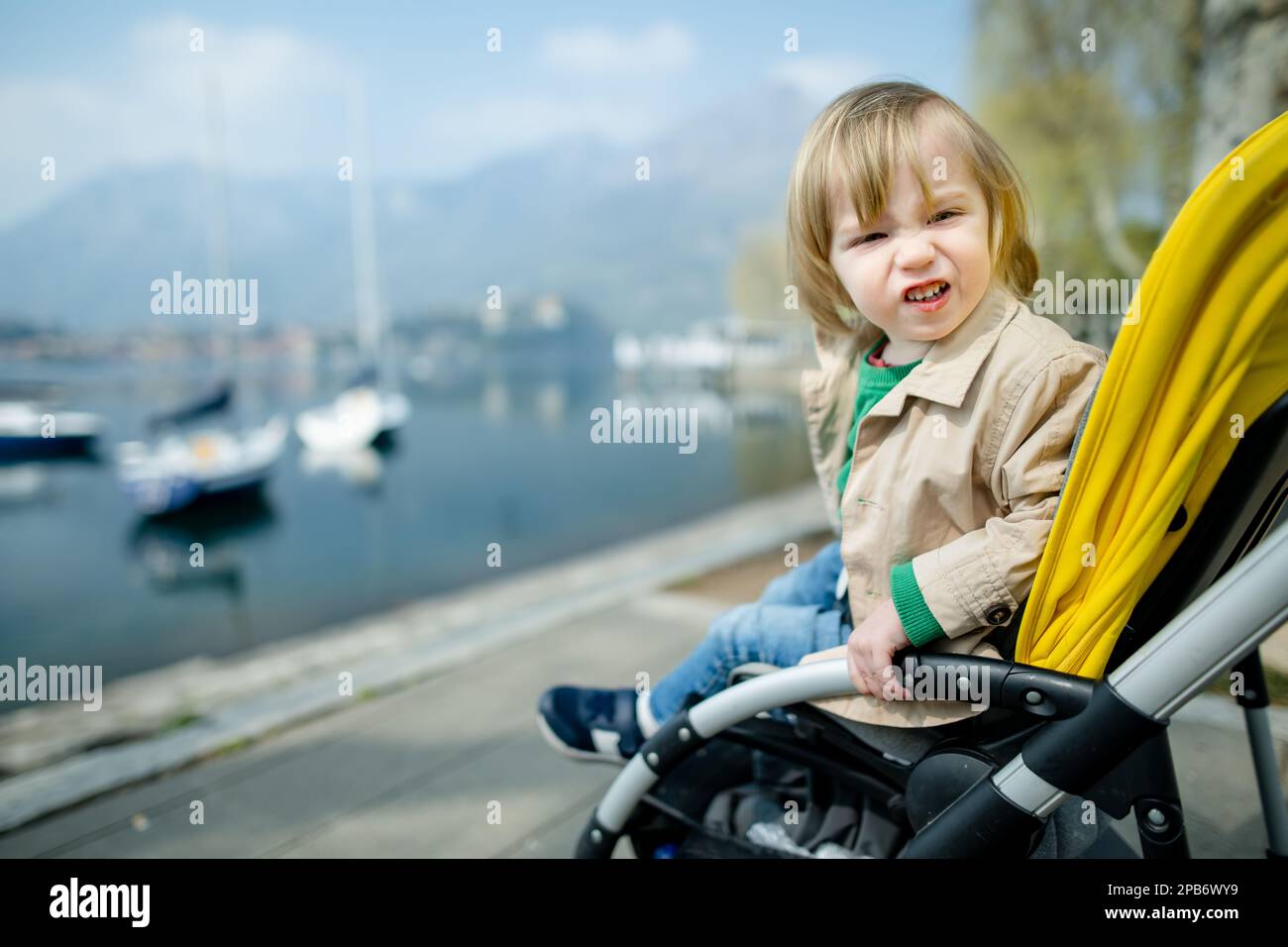 Funny toddler boy sitting in a stroller in Lecco town. Little child in ...