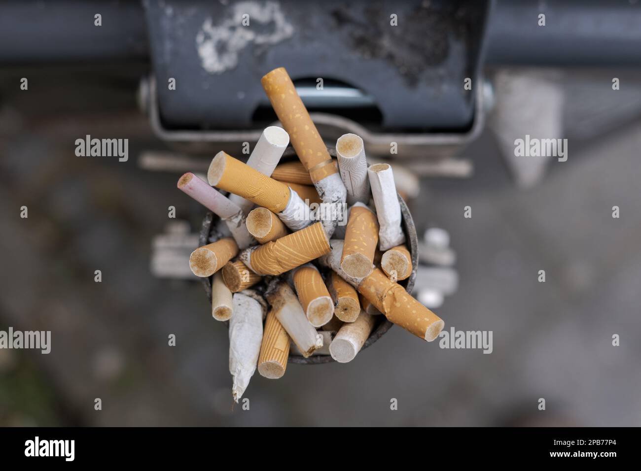 A lot of cigarette stubs stuffed into the pole of a trash can next to a ...