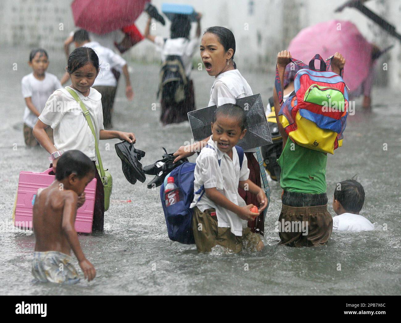 Filipino students wade thru flood waters as they walk outside their school in Manila ...