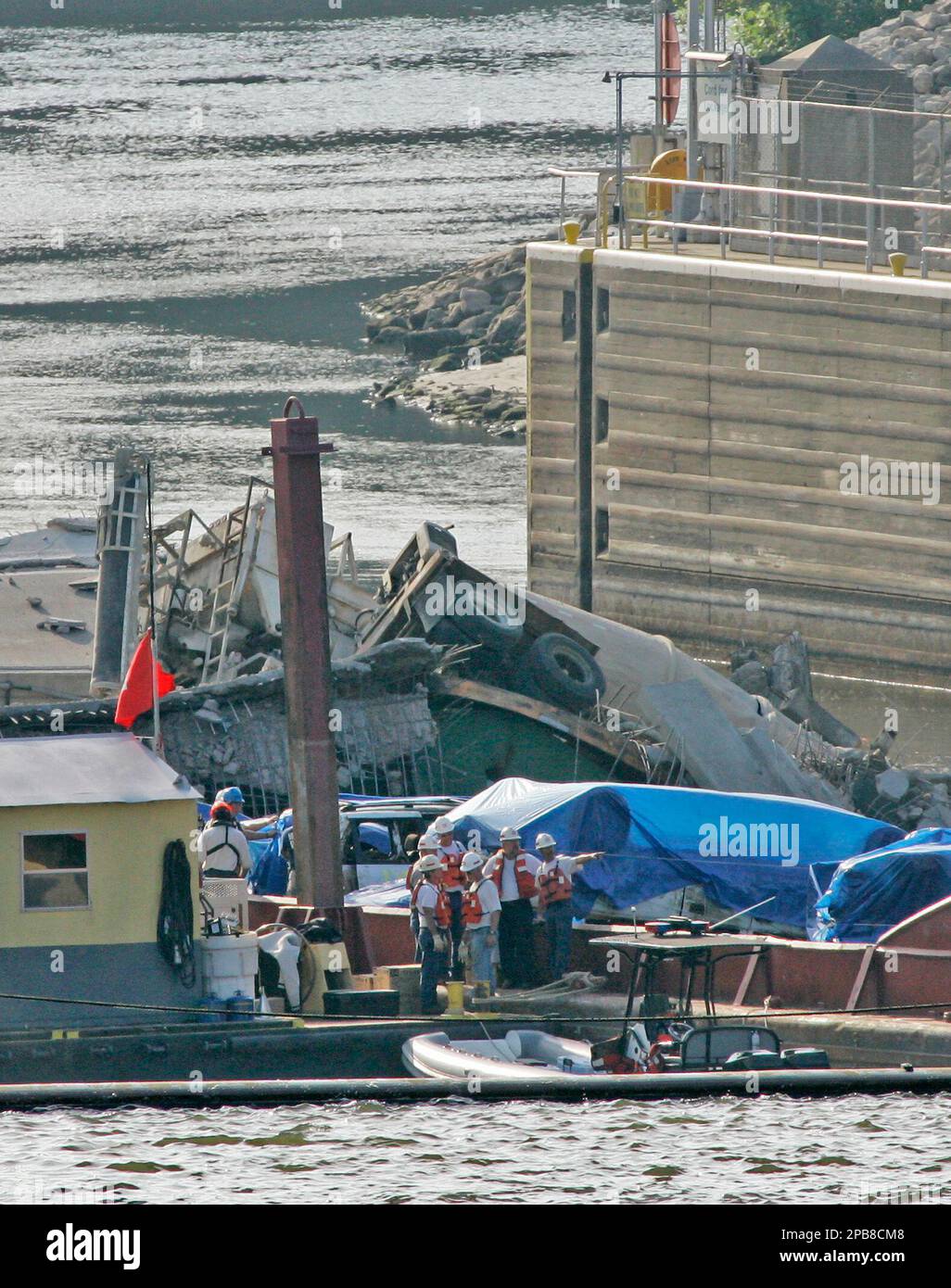 Rescue and salvage personnel work on a barge loaded with tarp-covered ...