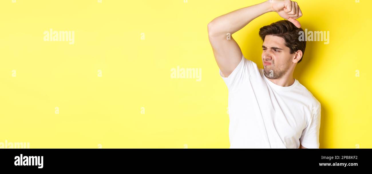 Man in sweat smelling his armpit, standing in white t-shirt and ...