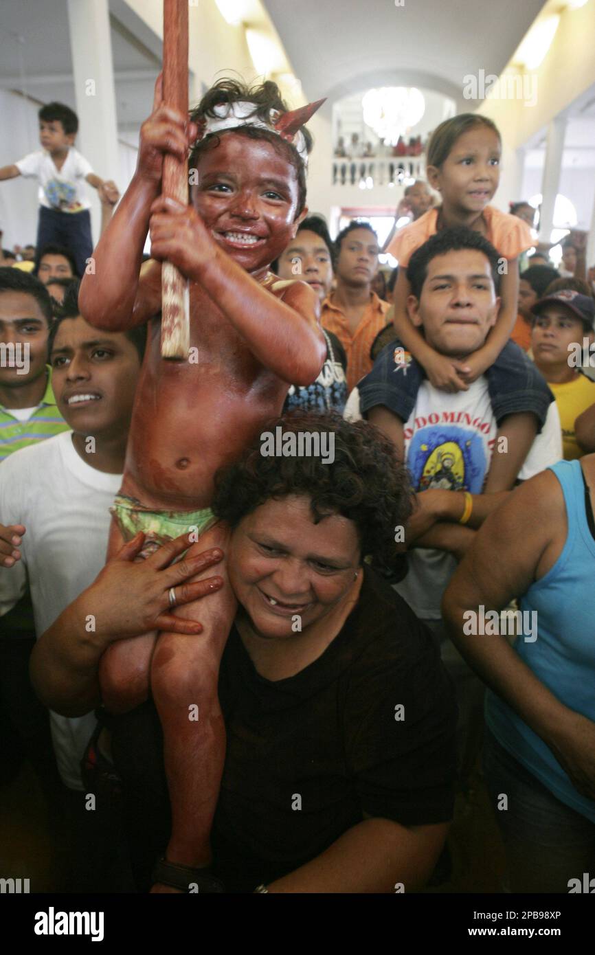 A child with his body painted in red and wearing devil's horns, is held ...