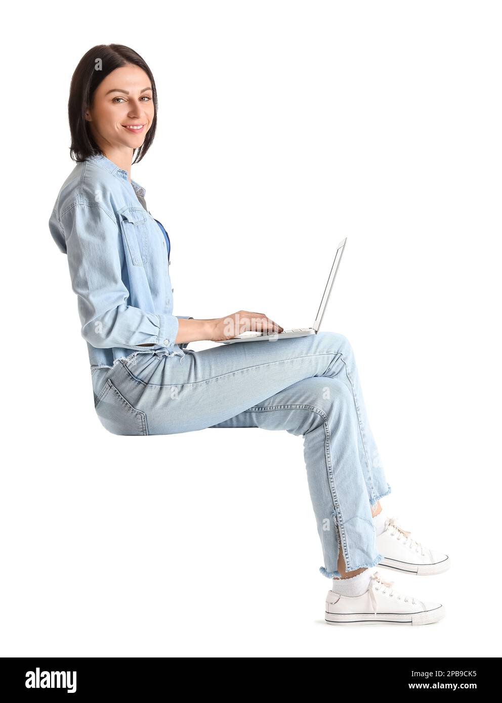 Pretty young woman with laptop sitting on chair against white ...