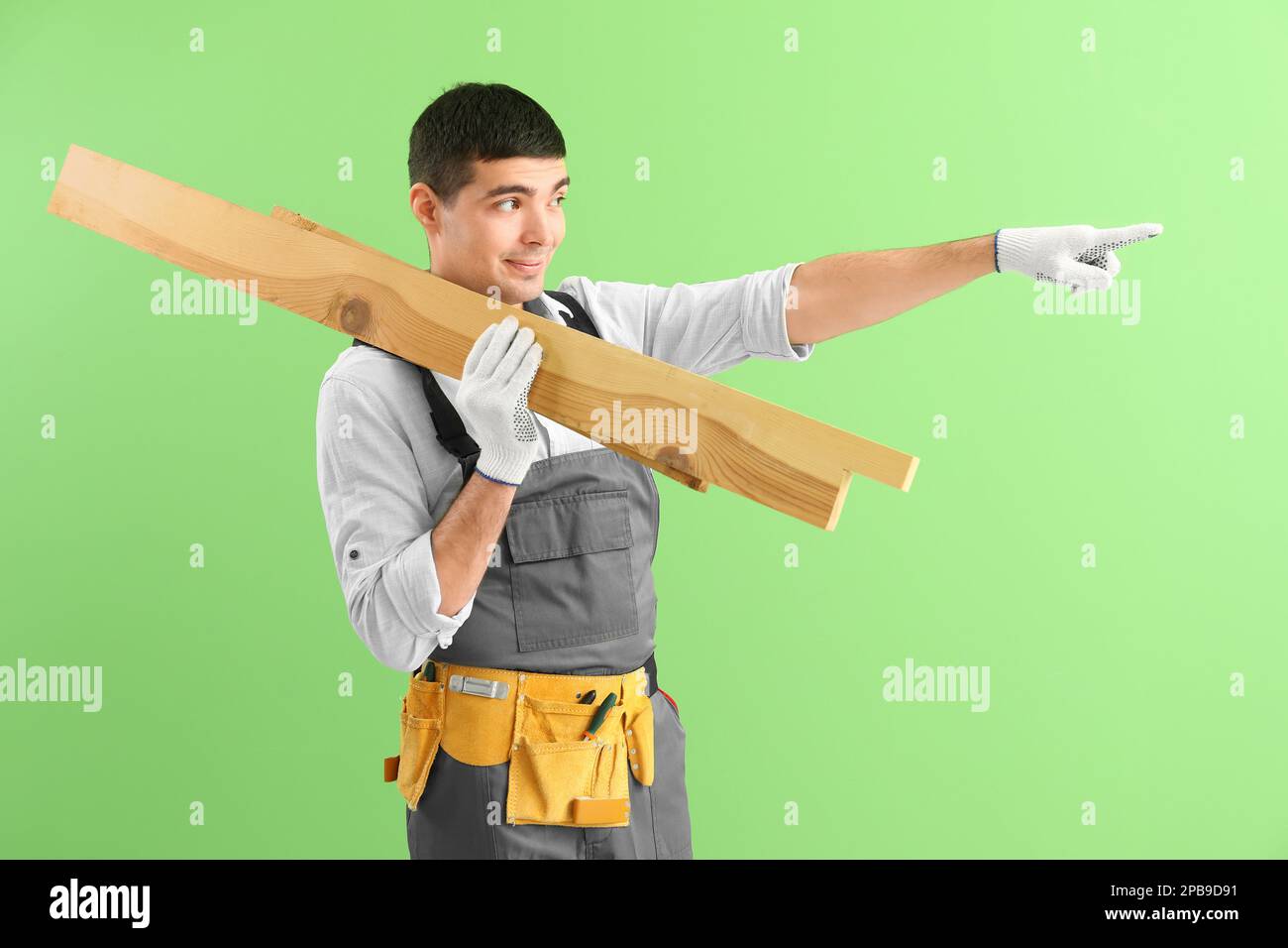 Young carpenter with wooden planks pointing at something on green ...