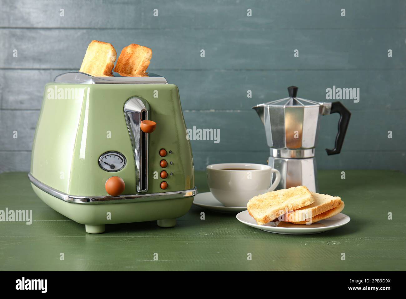 Modern toaster with crispy bread slices, geyser coffee maker and cup of espresso on green wooden ...